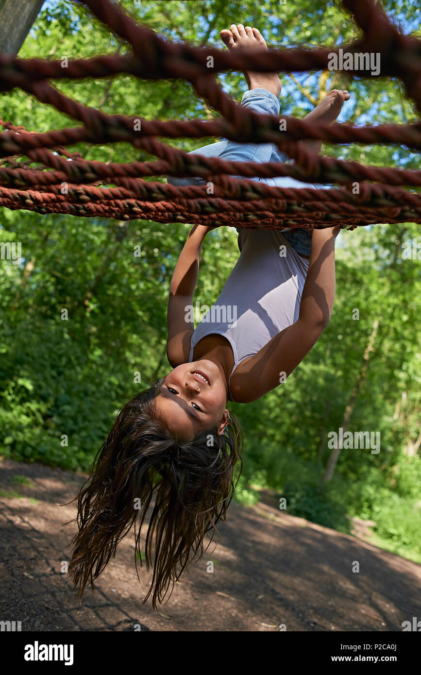 Cute young preteen Asian girl hanging upside down on some ropes in a ...
