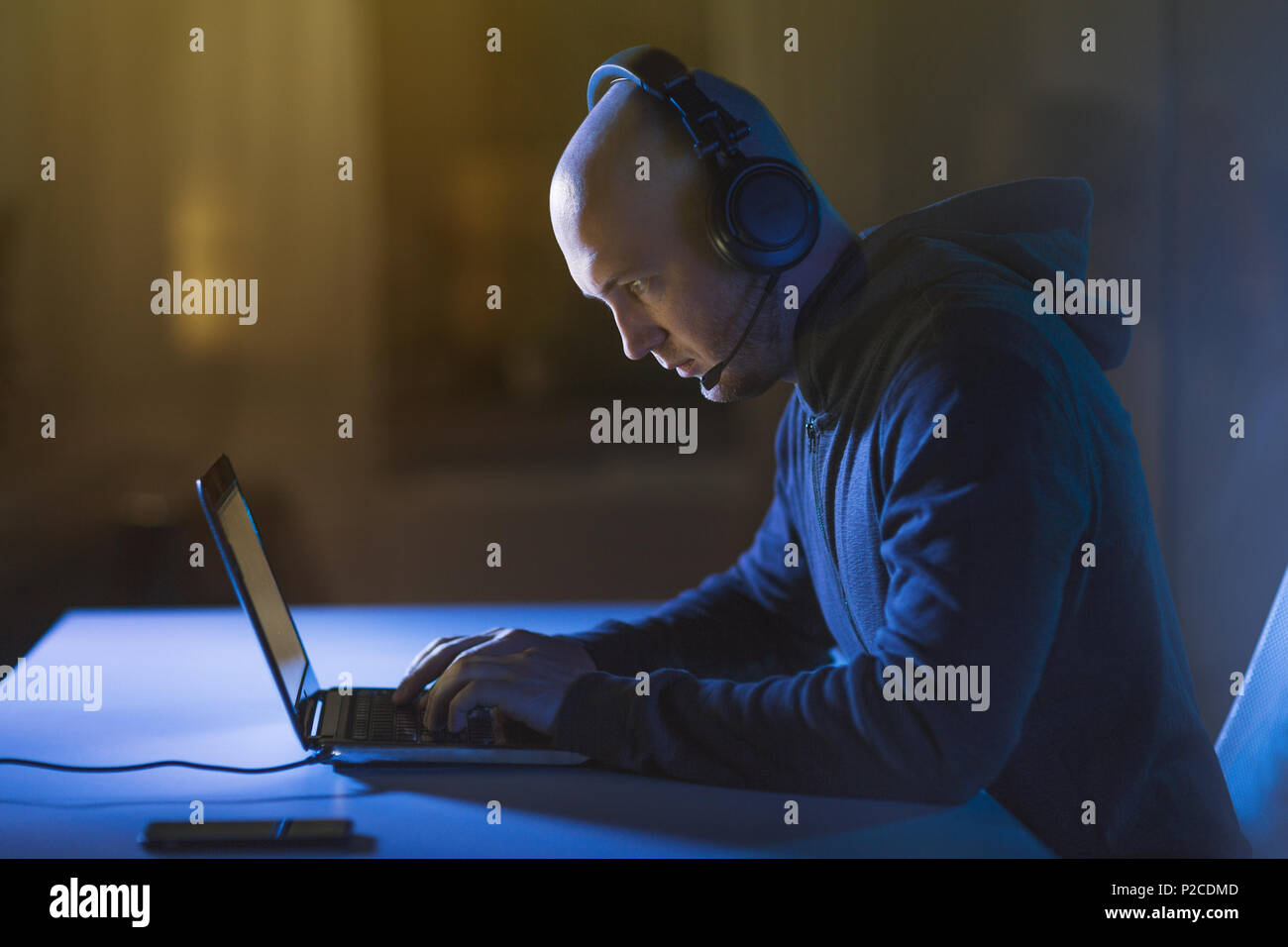 hacker in headset typing on laptop in dark room Stock Photo - Alamy