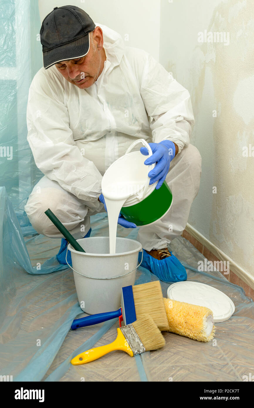 Painter paints the wall with the tint of white. Wall with serious ...