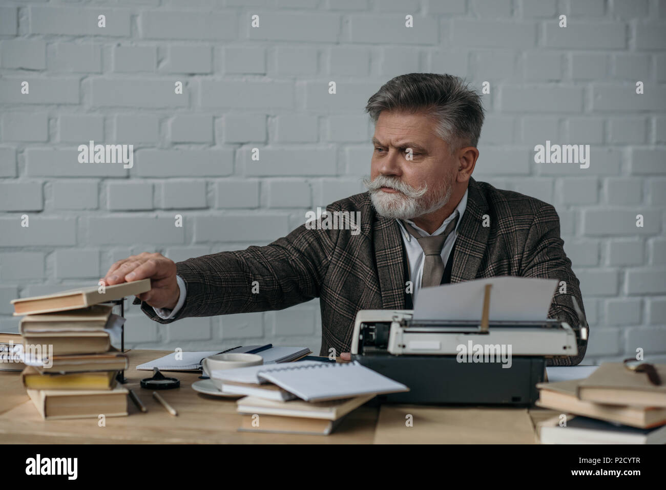 senior writer at workplace taking book from stack Stock Photo - Alamy