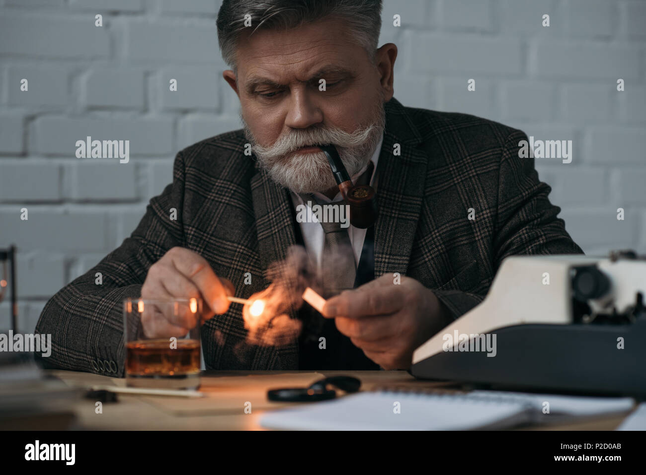 bearded senior writer with burning match smoking pipe at workplace ...