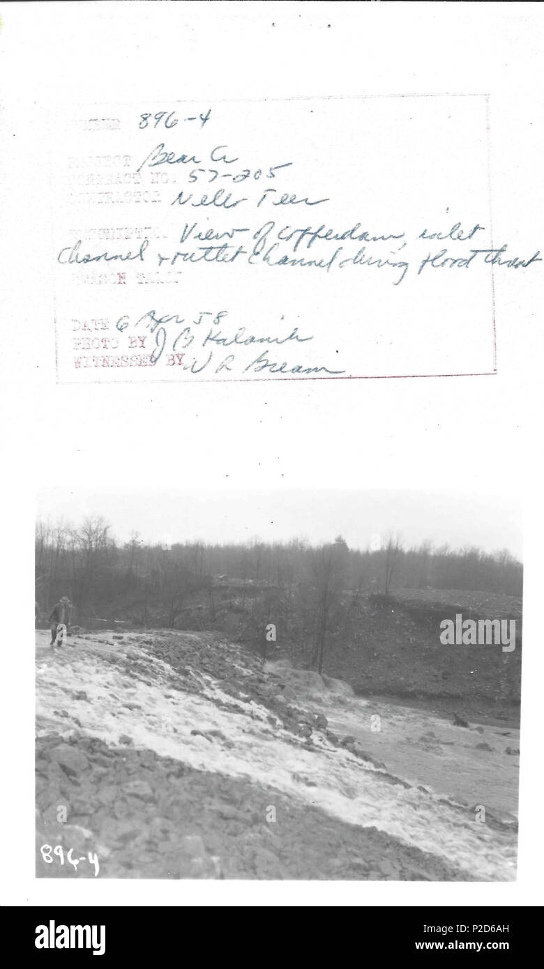 . English: A worker watches as water flows over the levee into the ...