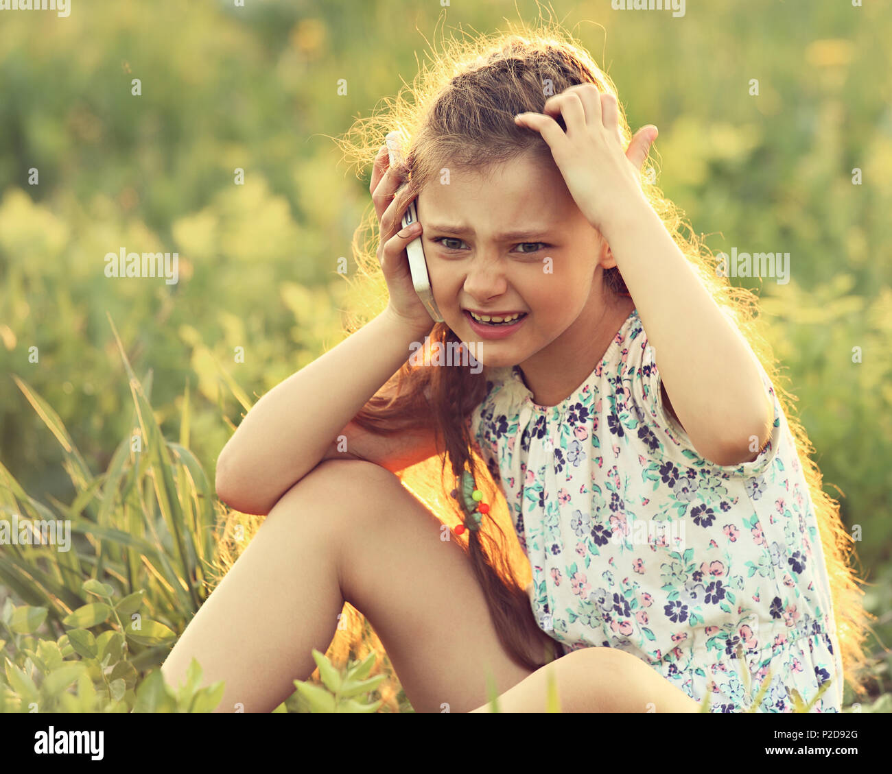 Angry serious cute kid girl sitting on the glass, talking on mobile ...