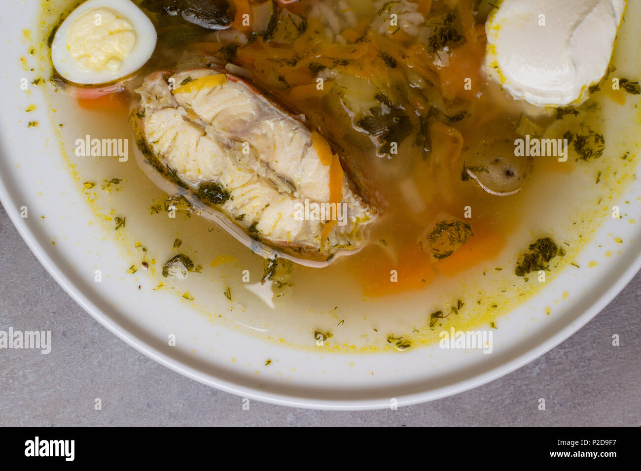 Fish soup with vegetables, rice, herbs and small eggs in white plate ...