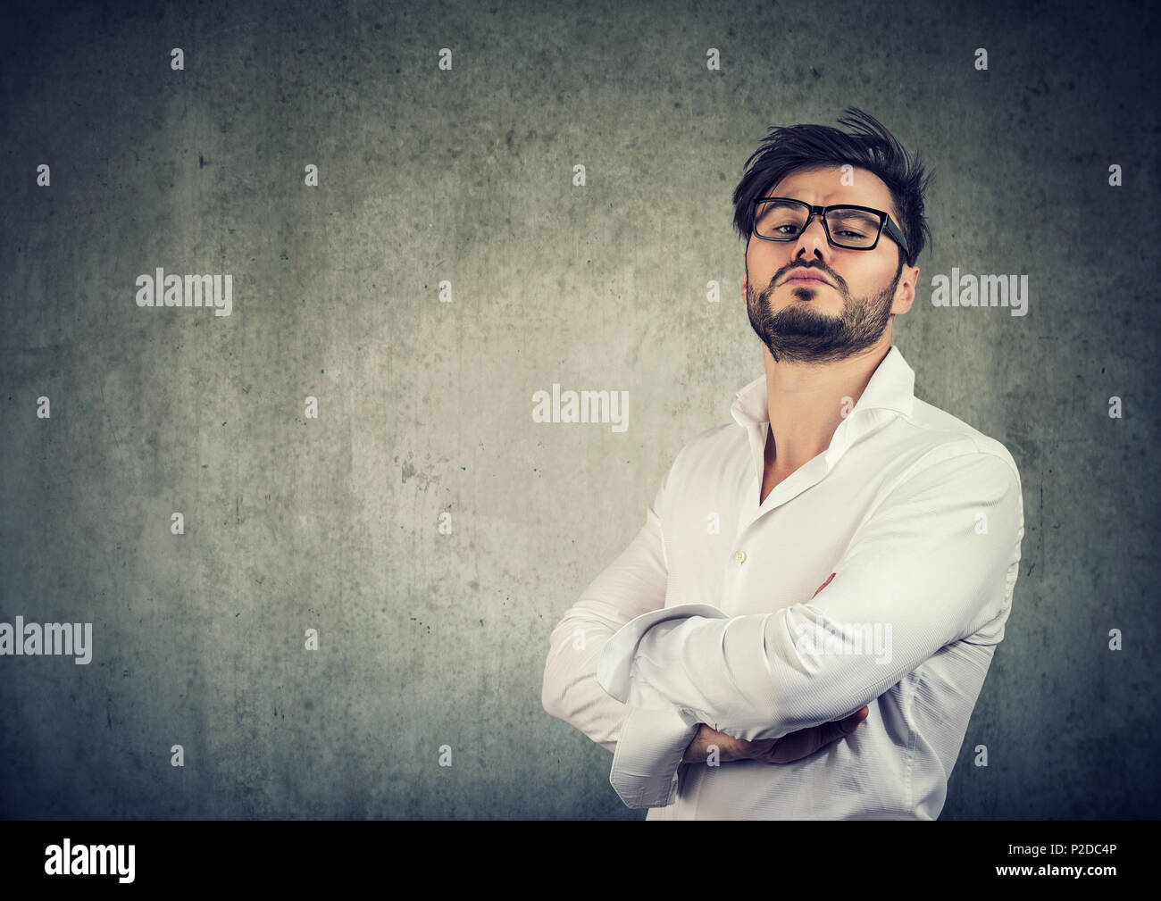 Young egocentric man in glasses holding hands crossed and looking ...