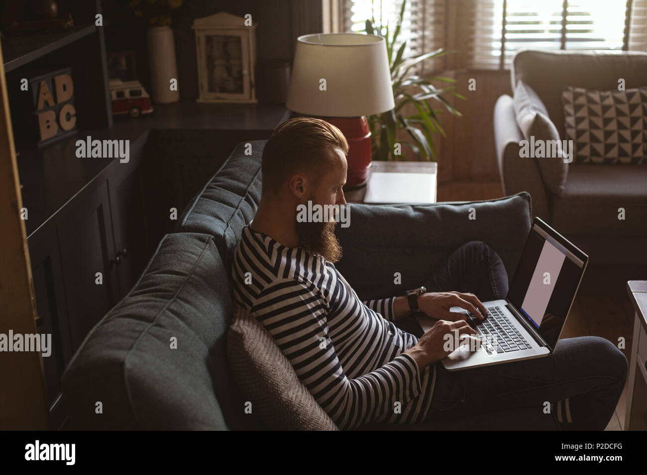 Man sitting on sofa using his laptop Stock Photo - Alamy