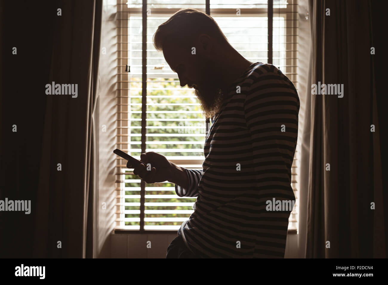 Man standing near window using his mobile phone Stock Photo - Alamy