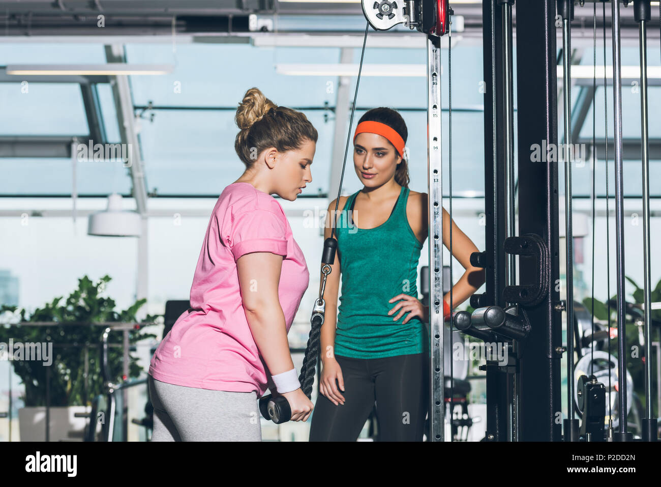 overweight woman working out on training apparatus while trainer ...