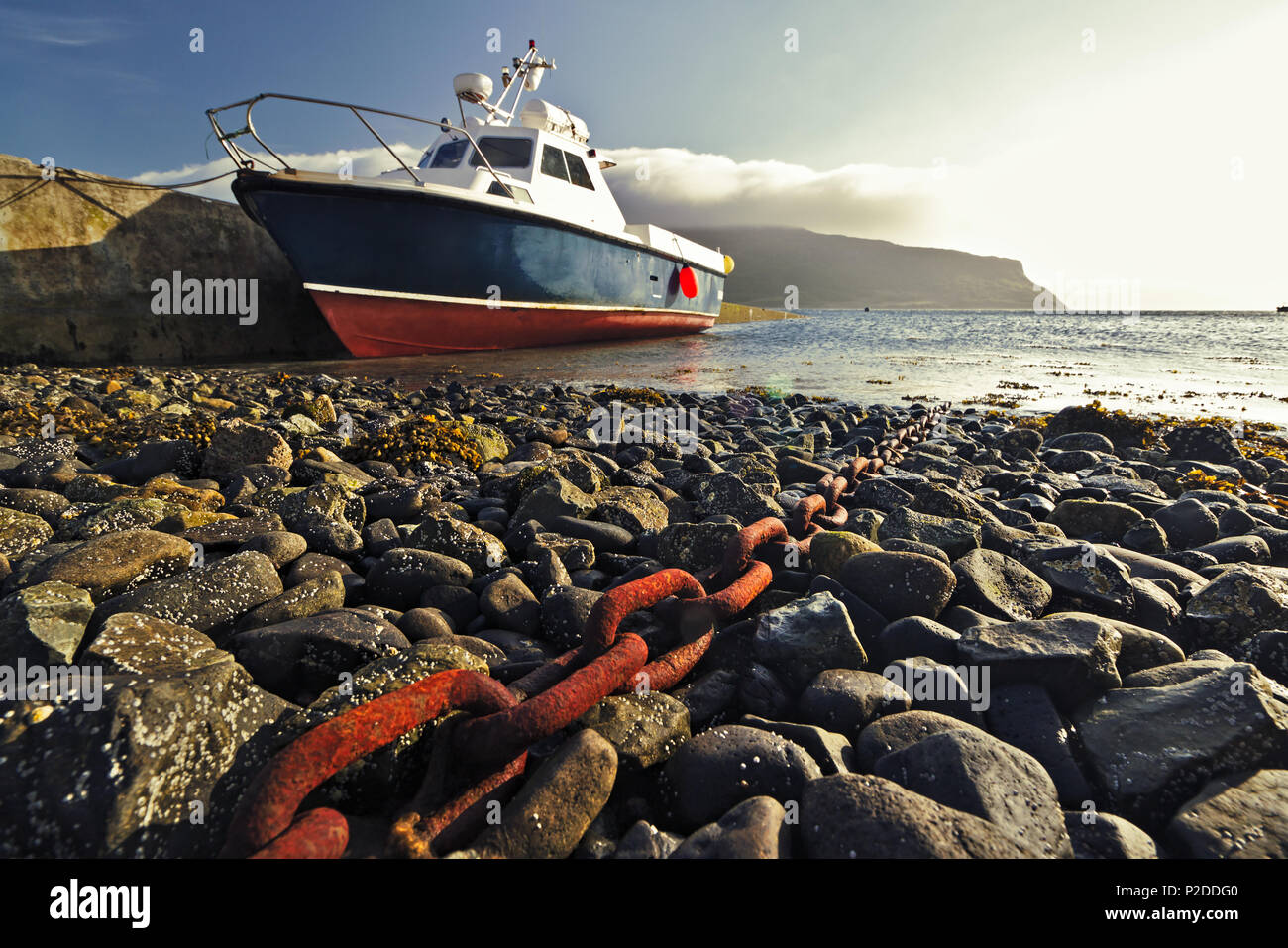 Boot moored at a jetty with pebble beach and red rusty chain leading ...