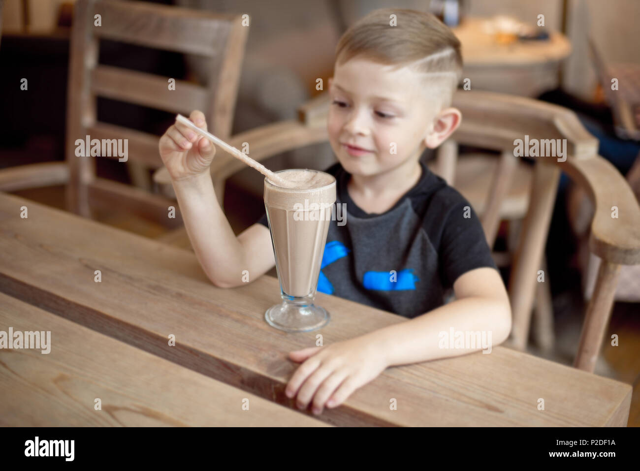 little boy drinking milkshake sitting at the table in cafe Stock Photo ...