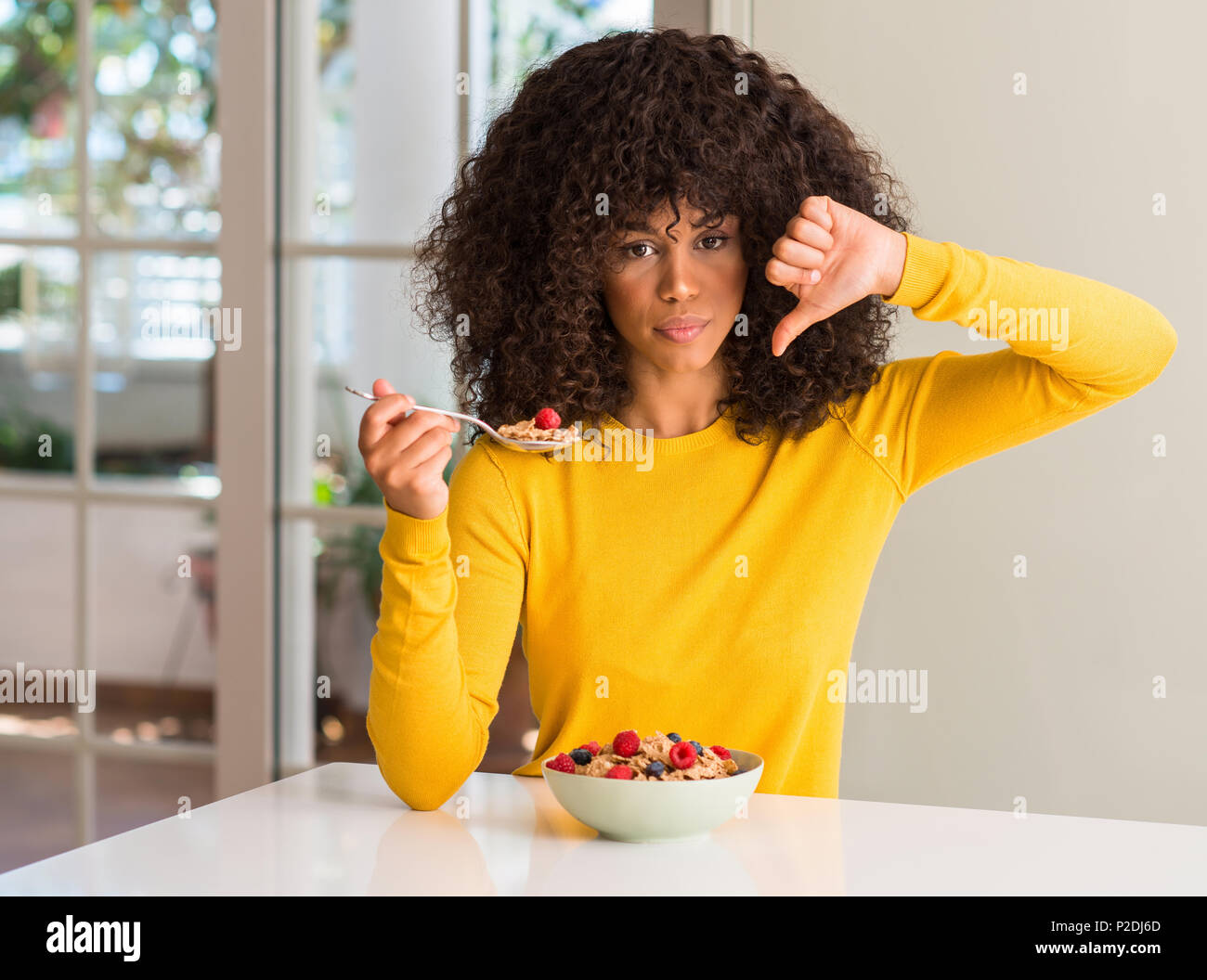 African american woman eating cereals, raspberries and blueberries with ...