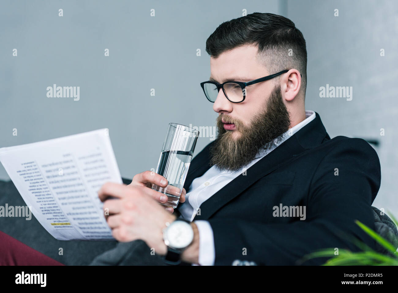 side view of focused businessman with glass of water in hand reading ...