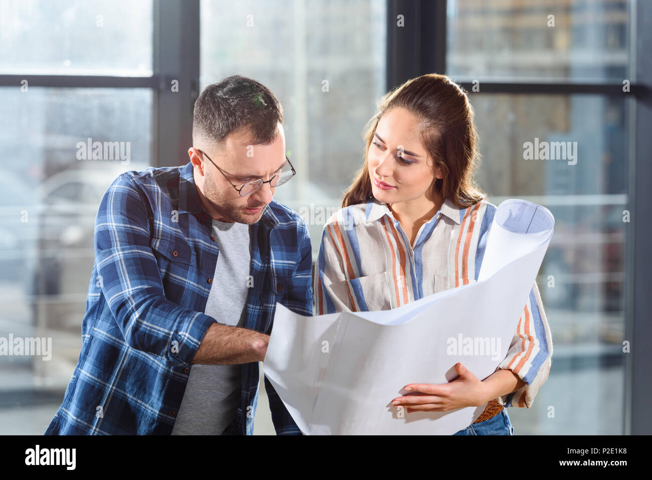 Female and male engineers looking at blueprint and discussing project ...