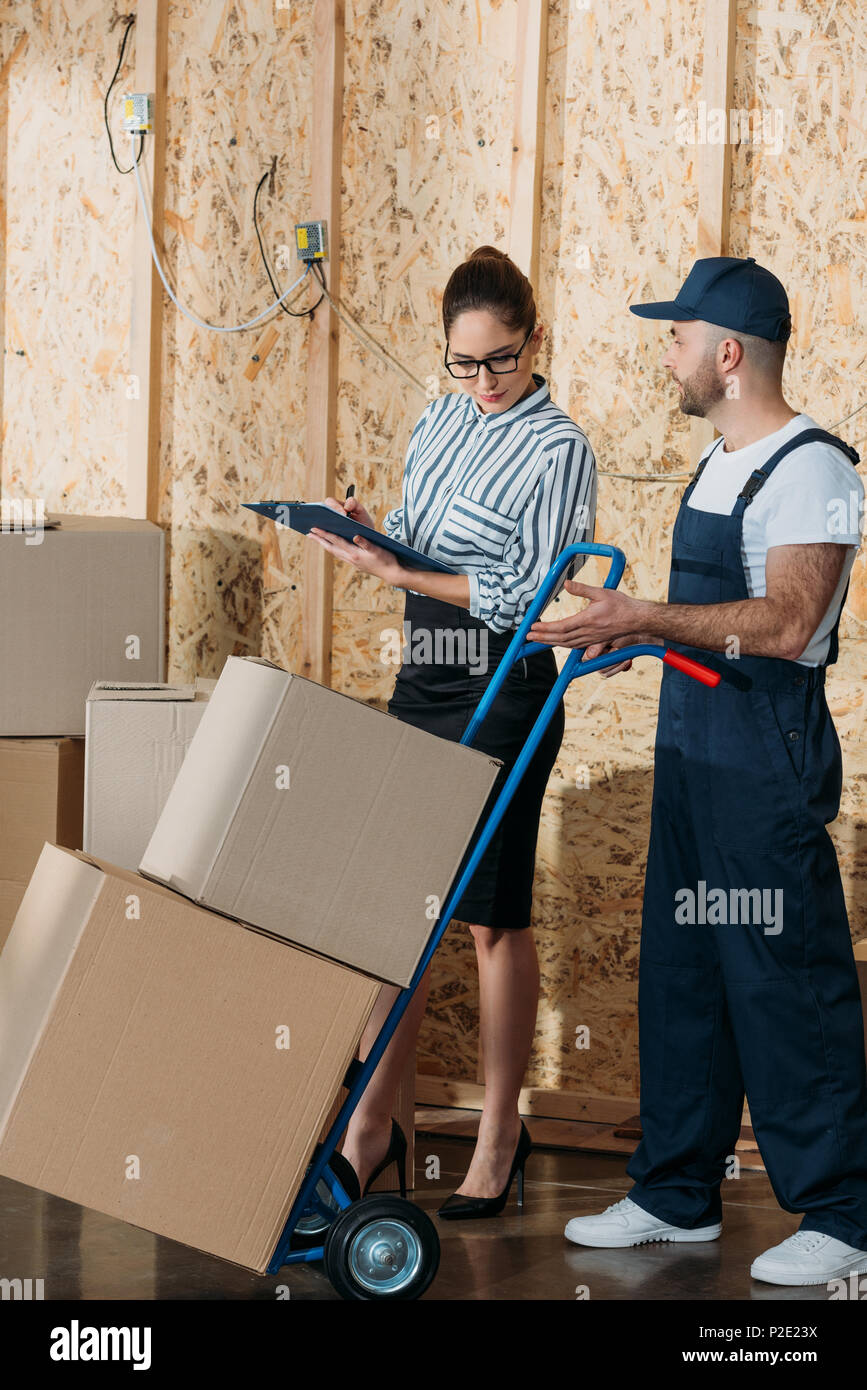 Businesswoman filling checklist while loader man carrying delivery cart ...