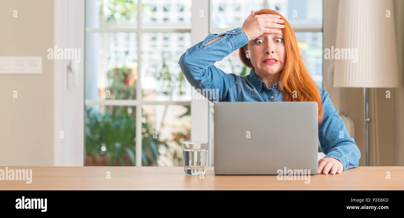 Redhead woman using computer laptop at home stressed with hand on head ...