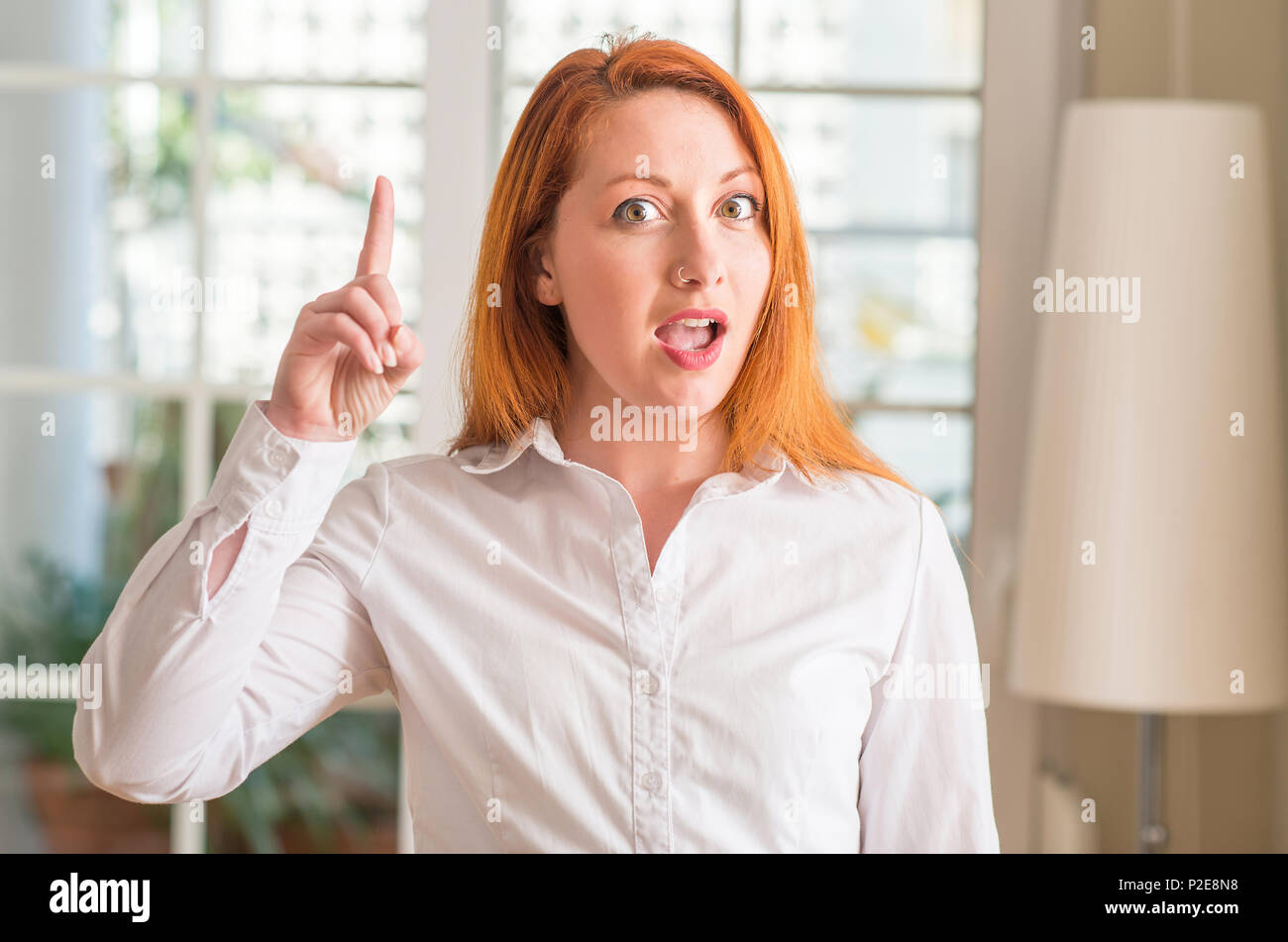 Redhead woman wearing white shirt at home surprised with an idea or ...