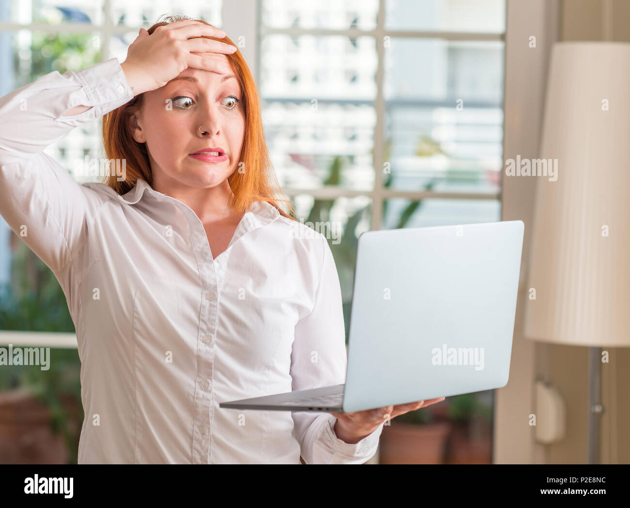 Redhead woman using computer laptop at home stressed with hand on head ...