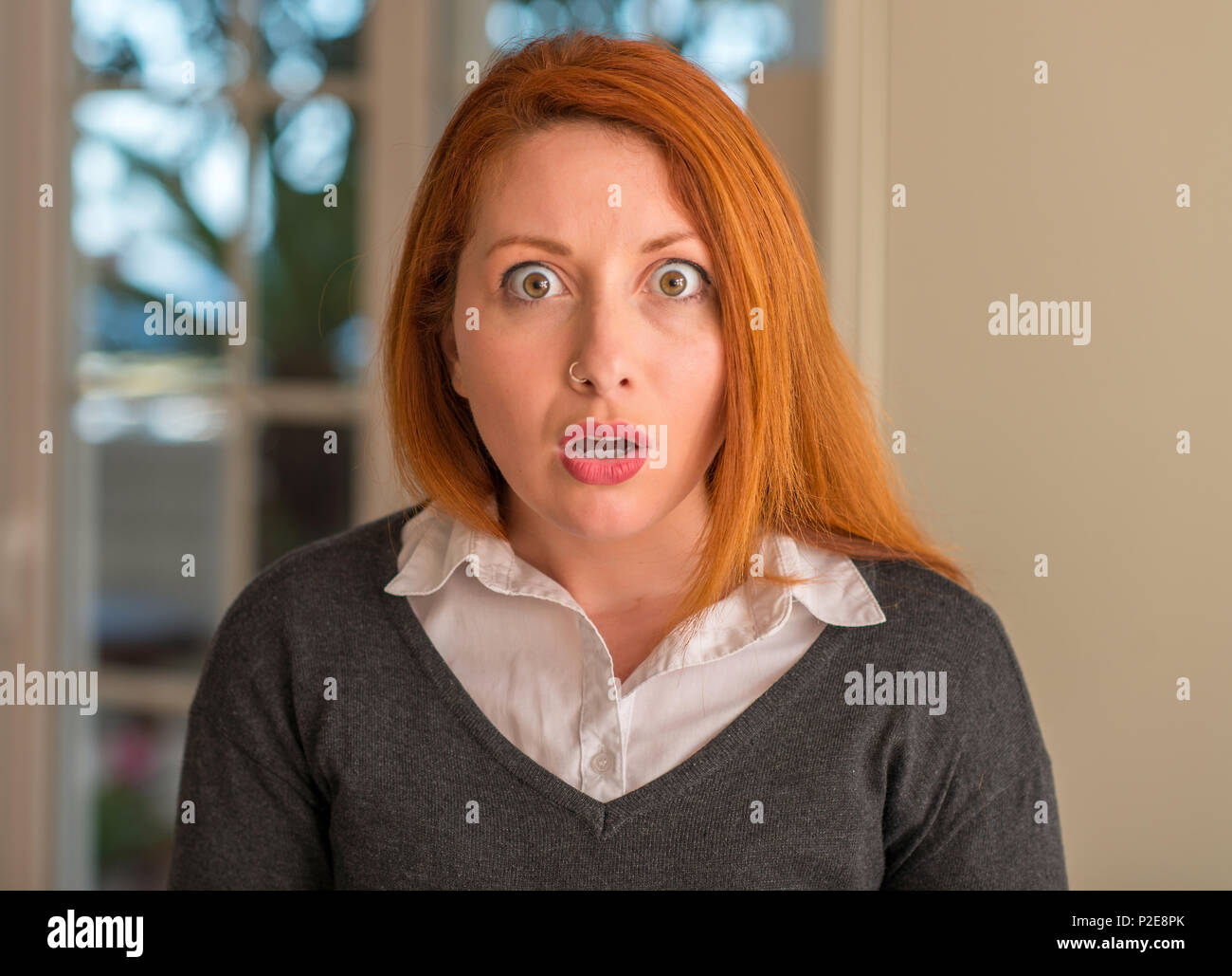 Redhead woman at home scared in shock with a surprise face, afraid and ...