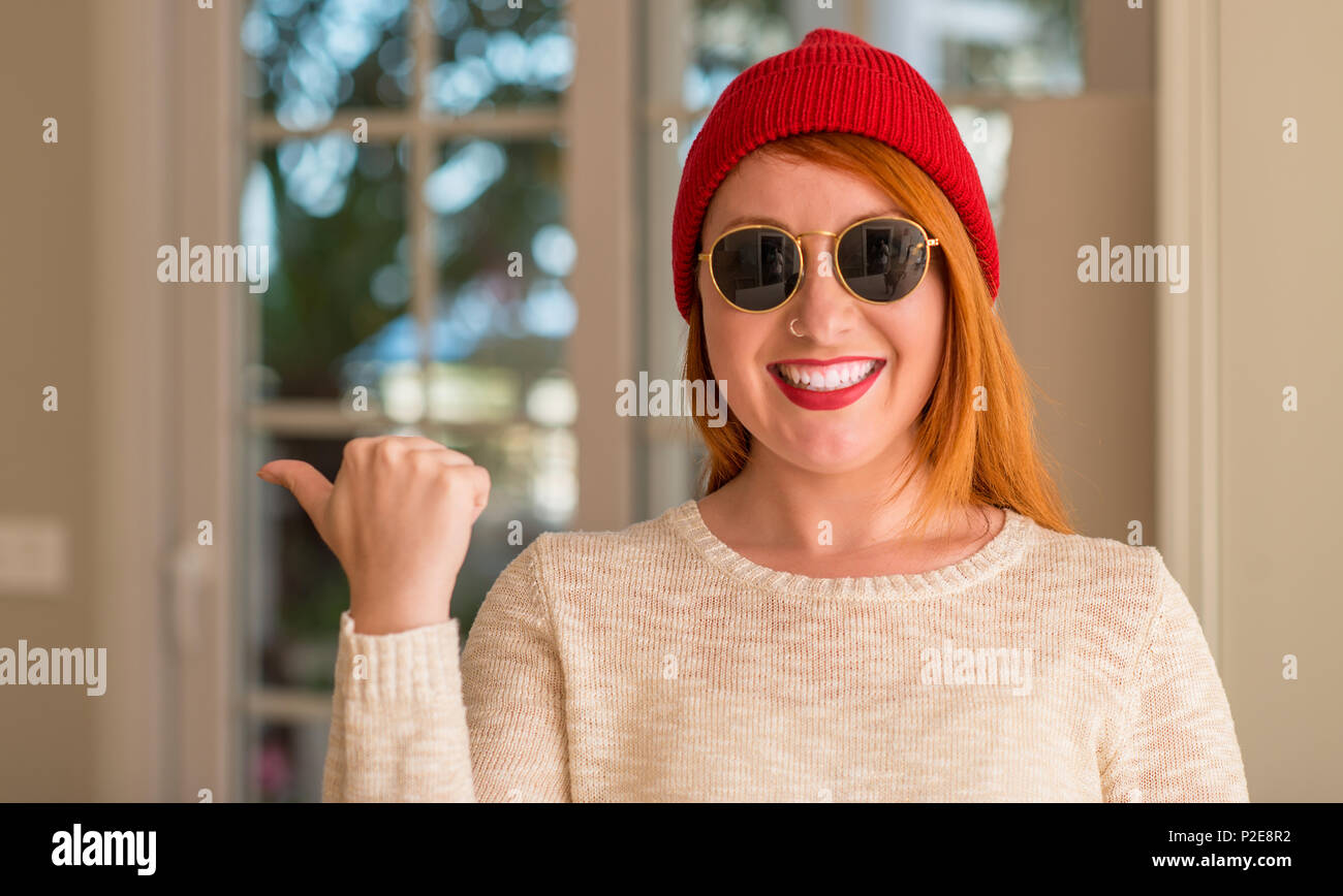 Stylish redhead woman wearing wool cap and sunglasses pointing with ...