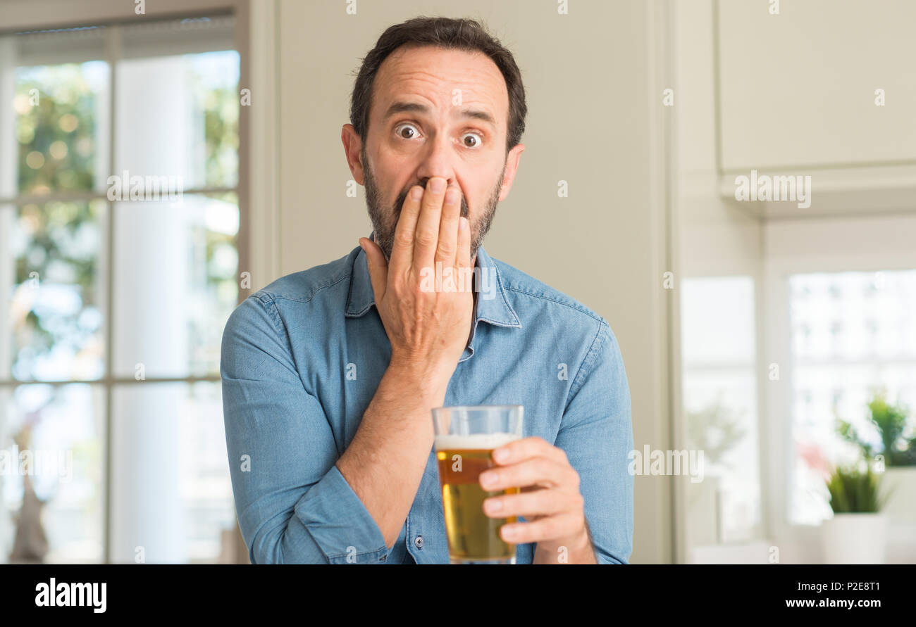 Middle age man drinking beer cover mouth with hand shocked with shame ...