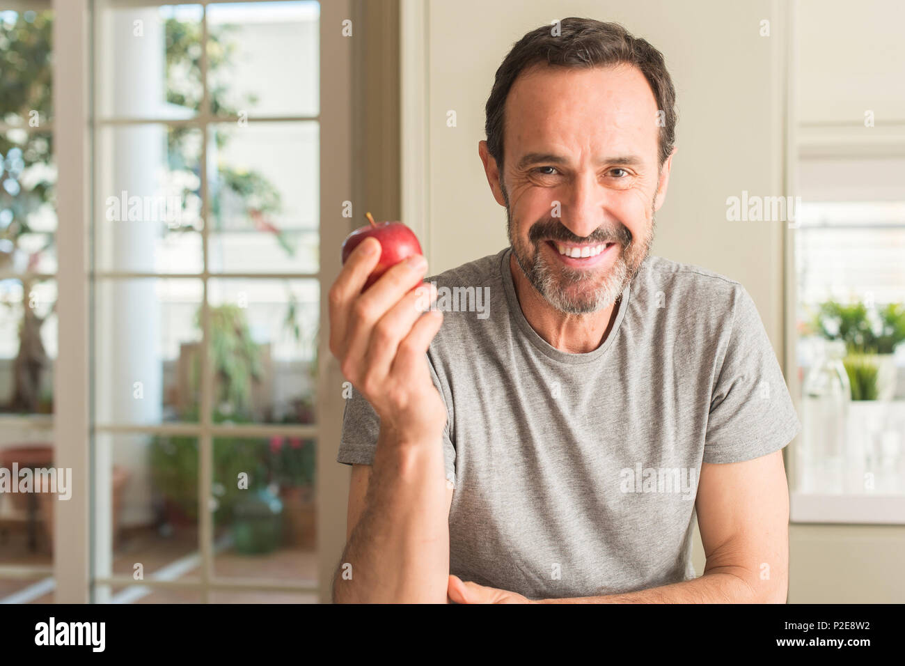 Middle age man eating healthy red apple with a happy face standing and ...