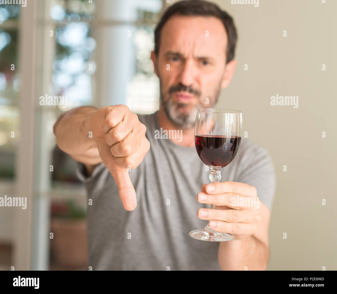 Middle age man drinking a glass of wine with angry face, negative sign ...