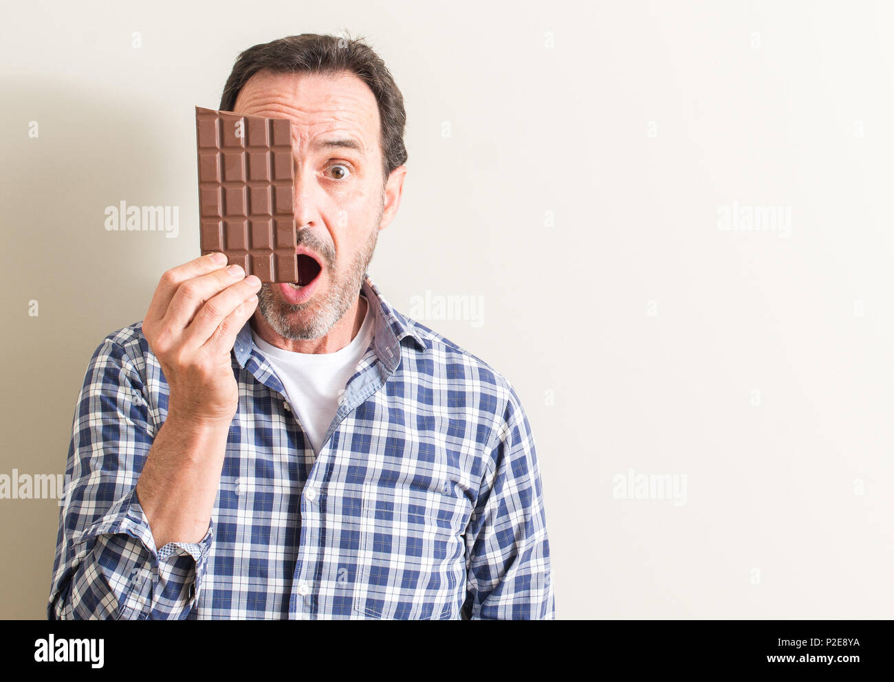 Senior man eating chocolate bar scared in shock with a surprise face ...