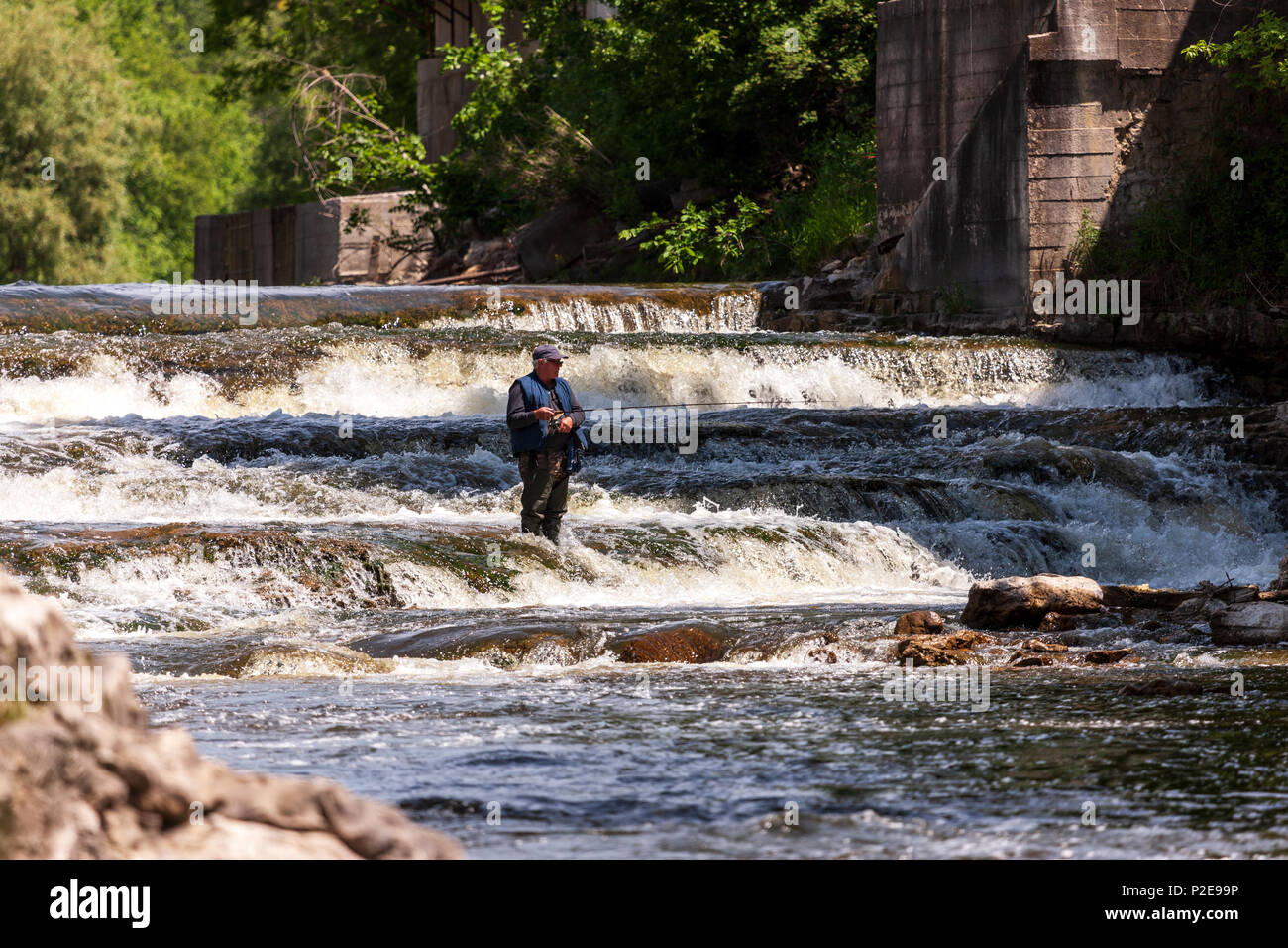 A man wearing hip waders fishes in the Grand River as it runs through ...