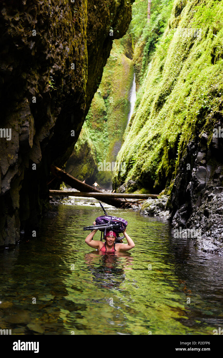 A woman carries her gear through the deep spot in the river trail to ...