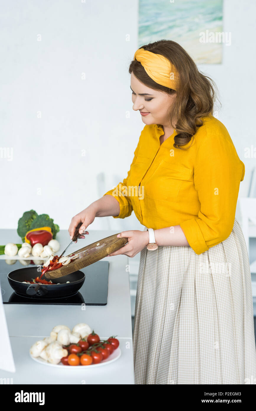 beautiful woman adding vegetables to frying pan at kitchen Stock Photo ...