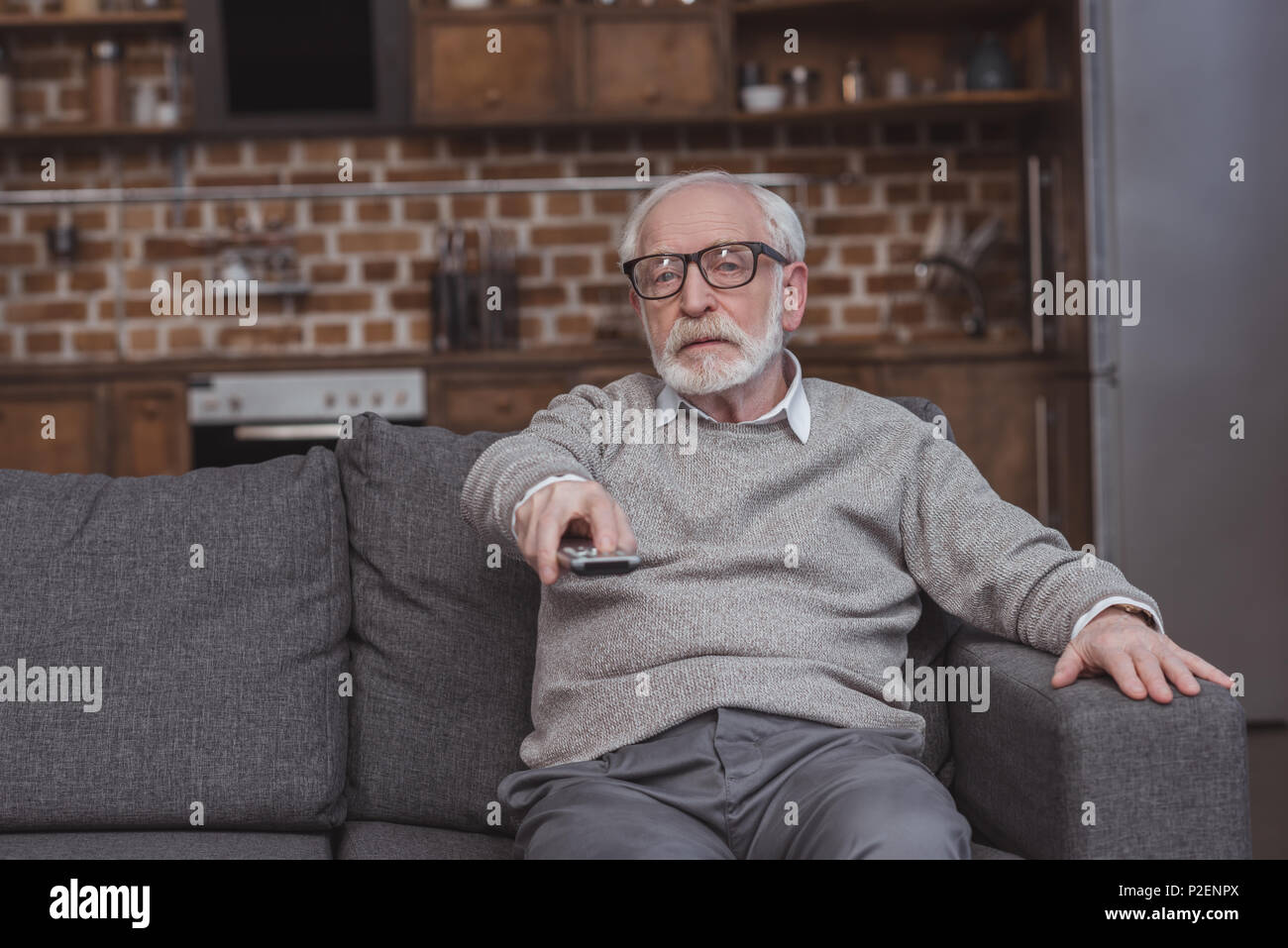 handsome grey hair man changing tv channels with remote control at home ...