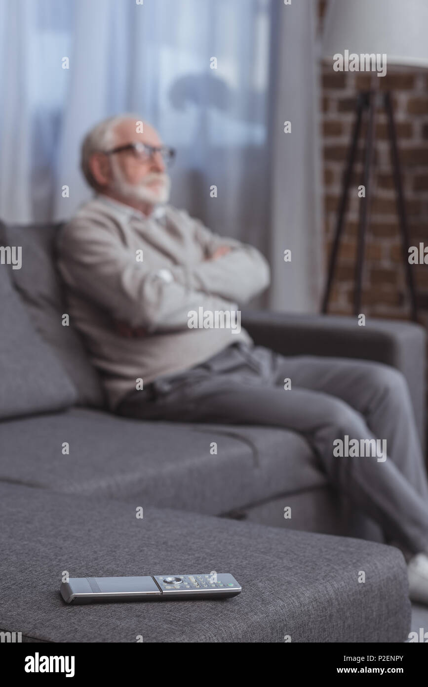handsome grey hair man sitting on sofa with crossed arms with remote ...