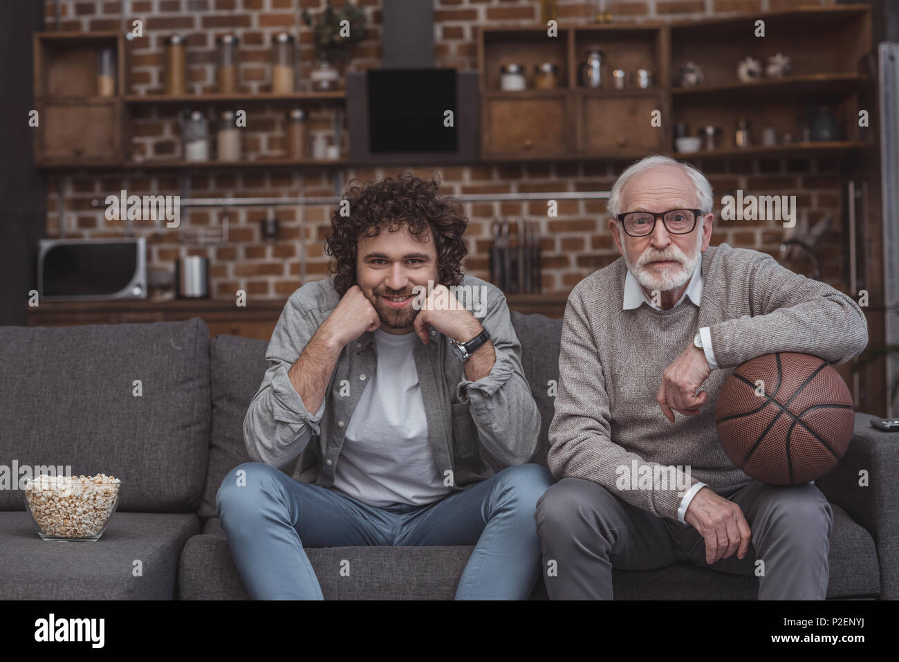 smiling adult son and senior father watching basketball game at home ...