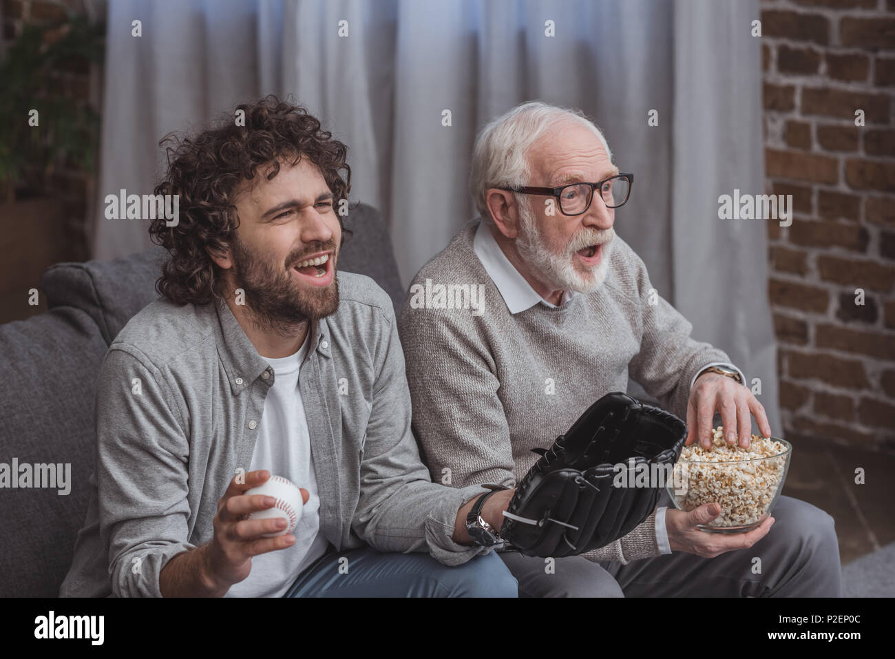 adult son and senior father cheering on baseball team and watching game ...