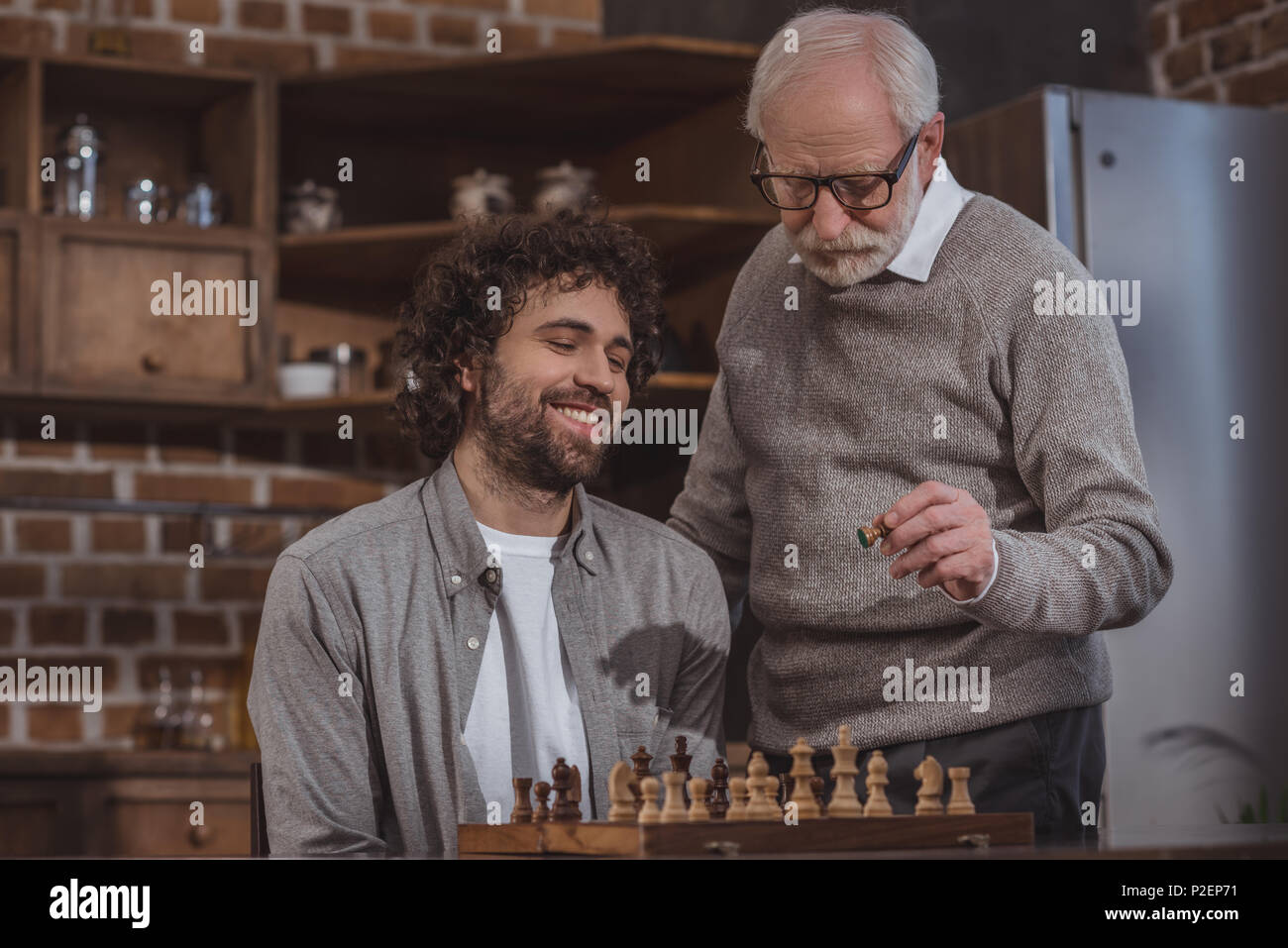 smiling adult son and senior father playing chess at home Stock Photo ...