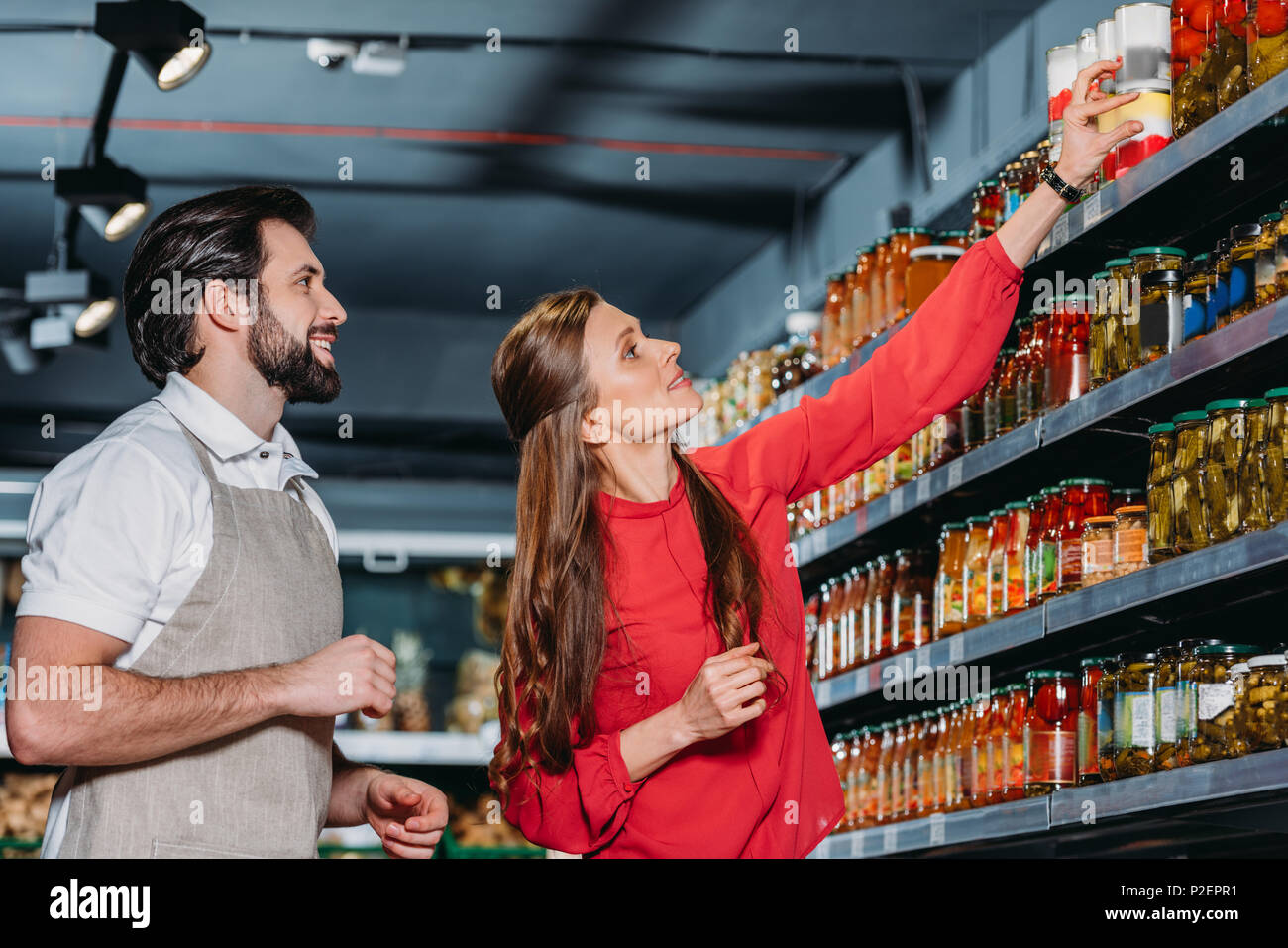 portrait of shop assistant in apron and female shopper in hypermarket ...