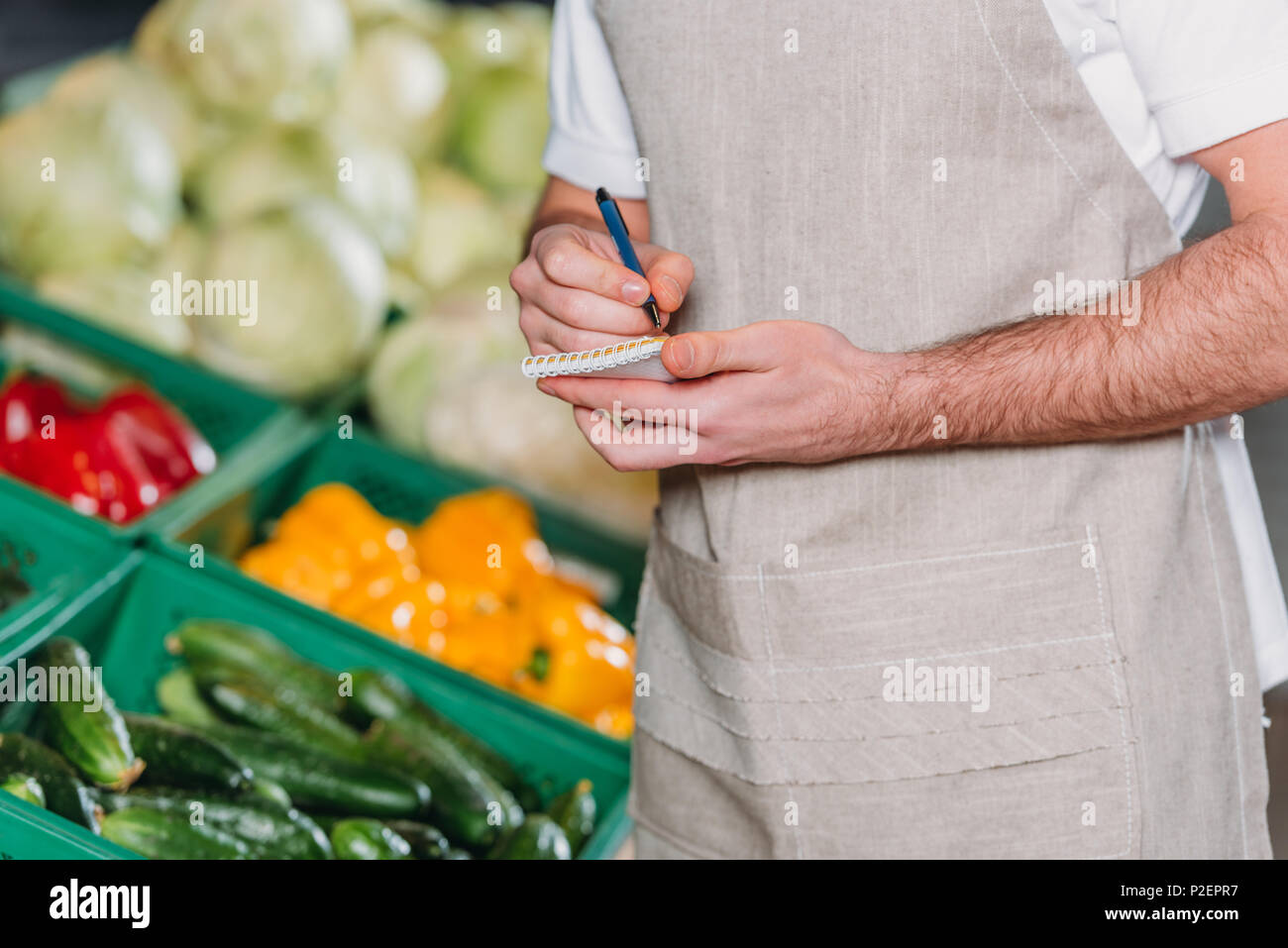partial view of shop assistant in apron making motes in notebook in ...