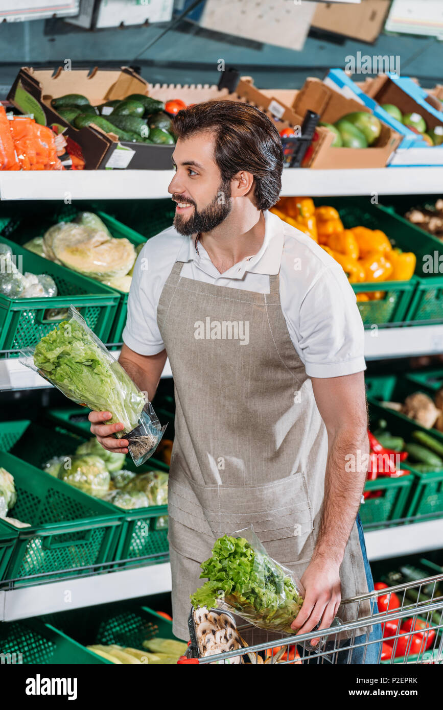 smiling shop assistant arranging fresh vegetables in grocery shop Stock ...