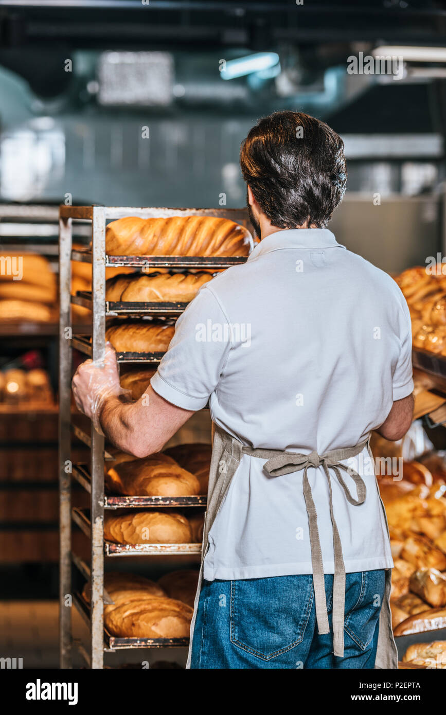 back view of shop assistant in apron arranging fresh pastry in ...
