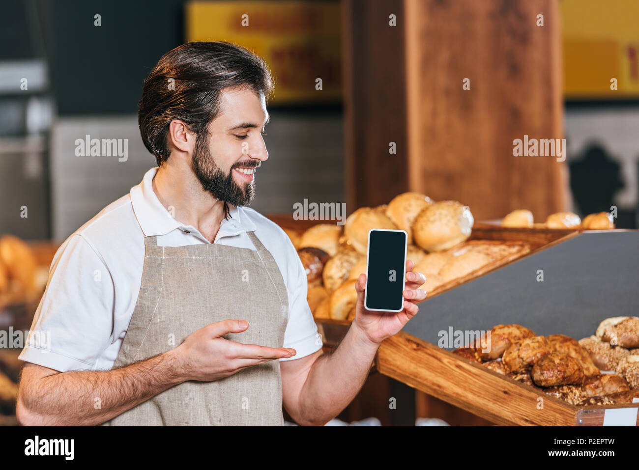 portrait of smiling shop assistant showing smartphone with blank screen ...