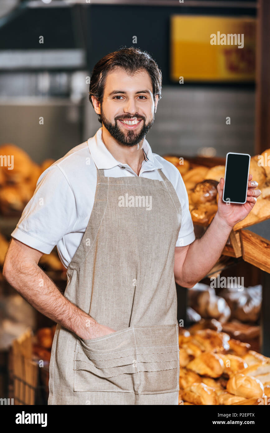 portrait of smiling shop assistant showing smartphone with blank screen ...