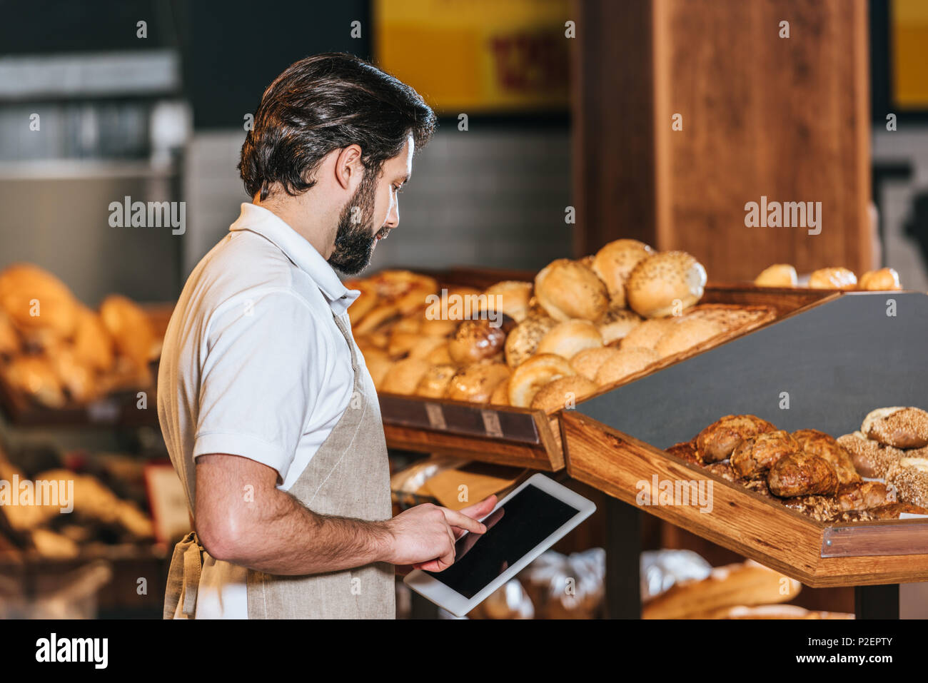 side view of shop assistant in apron using tablet with blank screen in ...