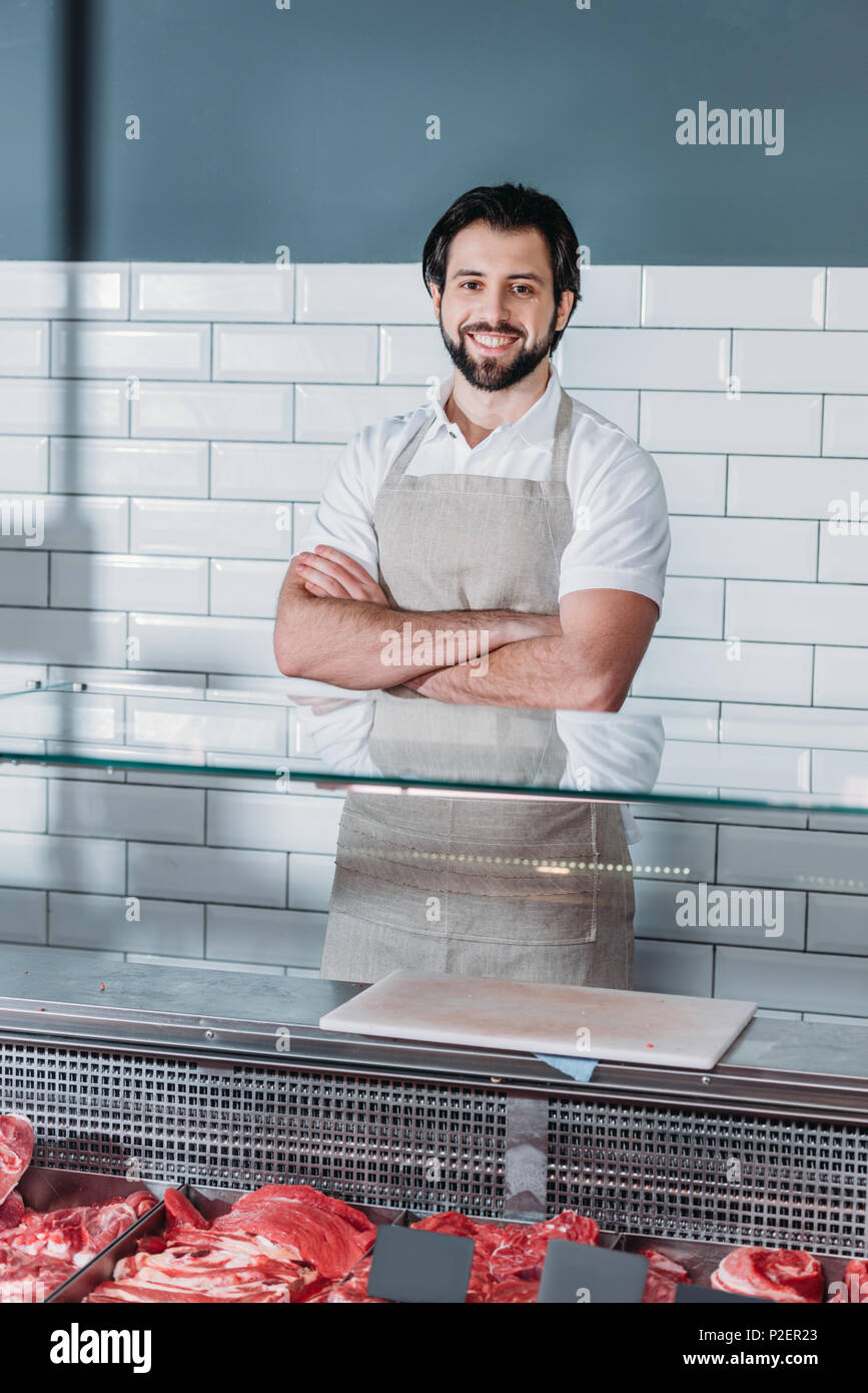 portrait of smiling shop assistant in apron with arms crossed standing ...