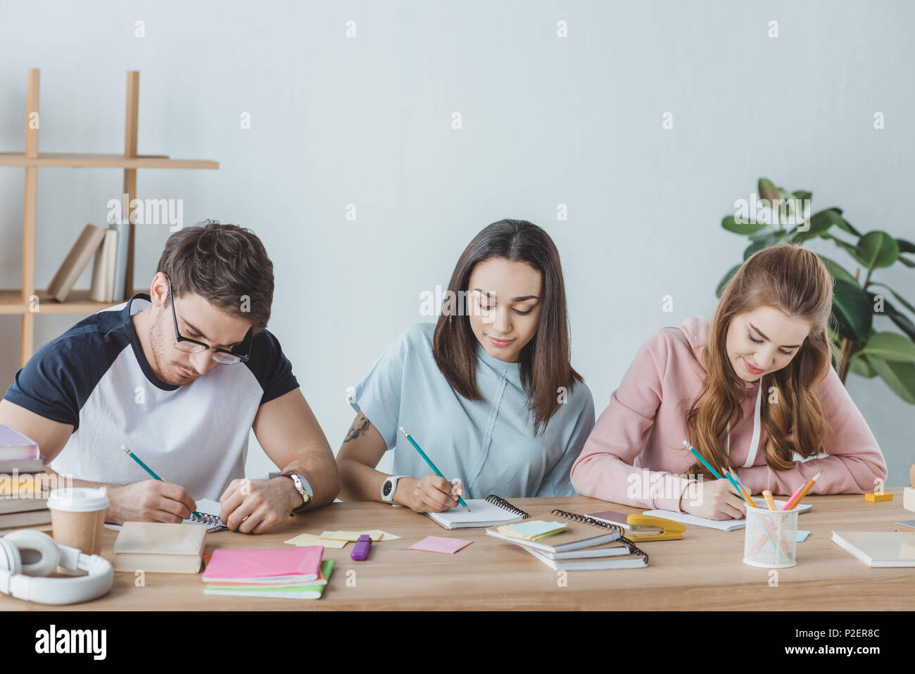 young multicultural students writing in copybooks at table Stock Photo ...