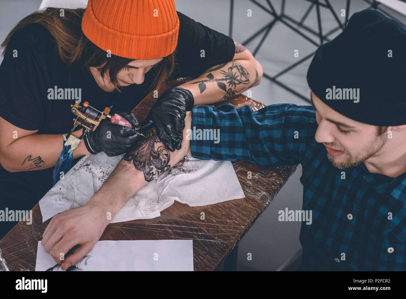 Young man and female tattoo master during tattoo process in studio ...