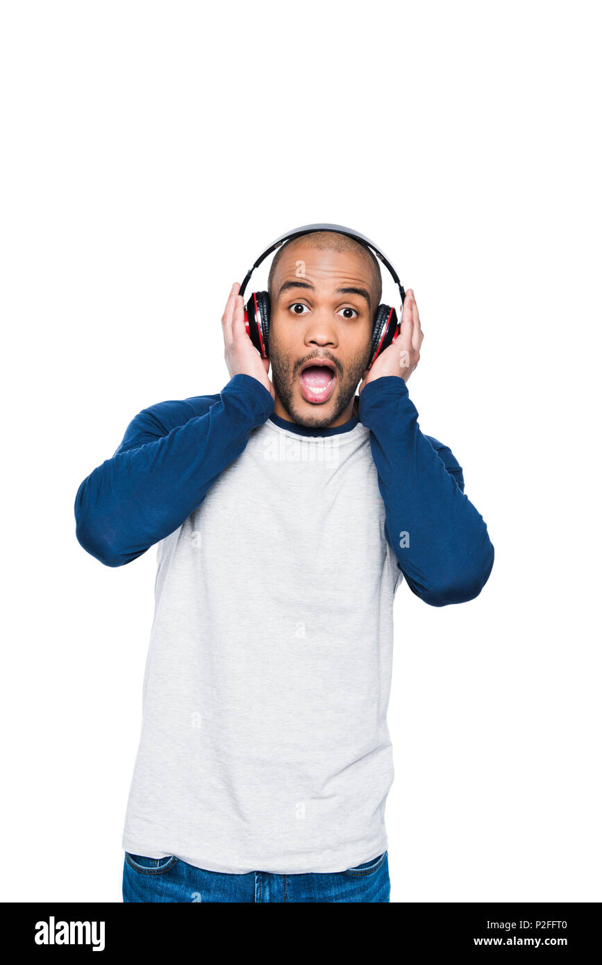 shocked young african american man listening music in headphones and looking at camera isolated ...