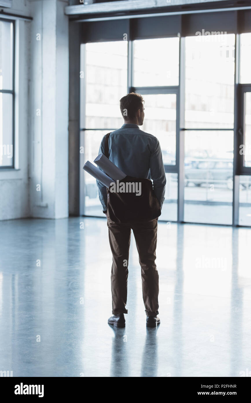 back view of architect with bag full of blueprints standing in empty ...