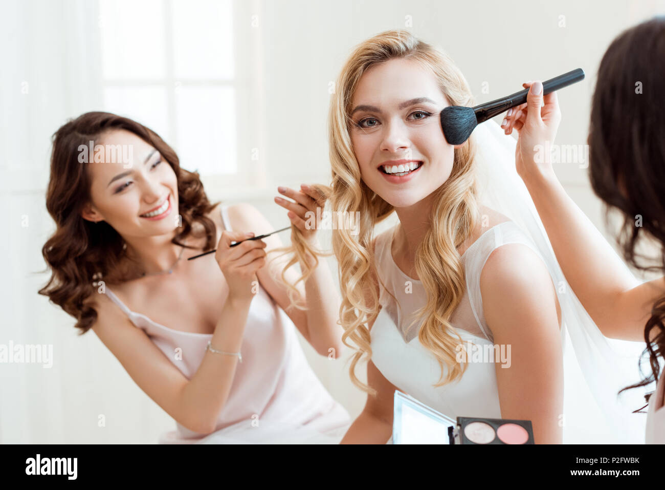 beautiful young bride getting makeup before wedding and looking at ...