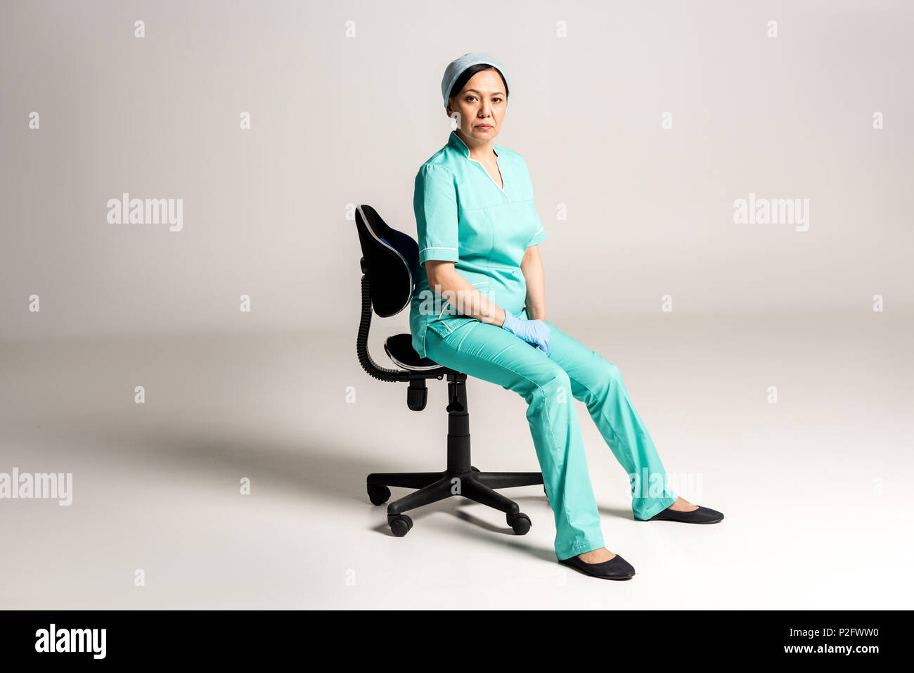 full length view of female asian doctor sitting on chair and looking at ...