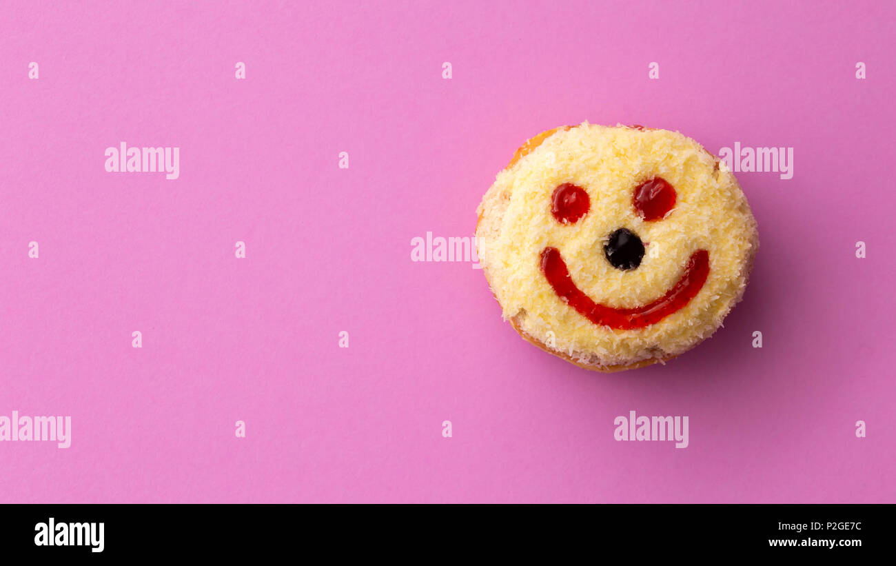 Close up flat lay of yellow smiley happy face donut isolated on pink ...